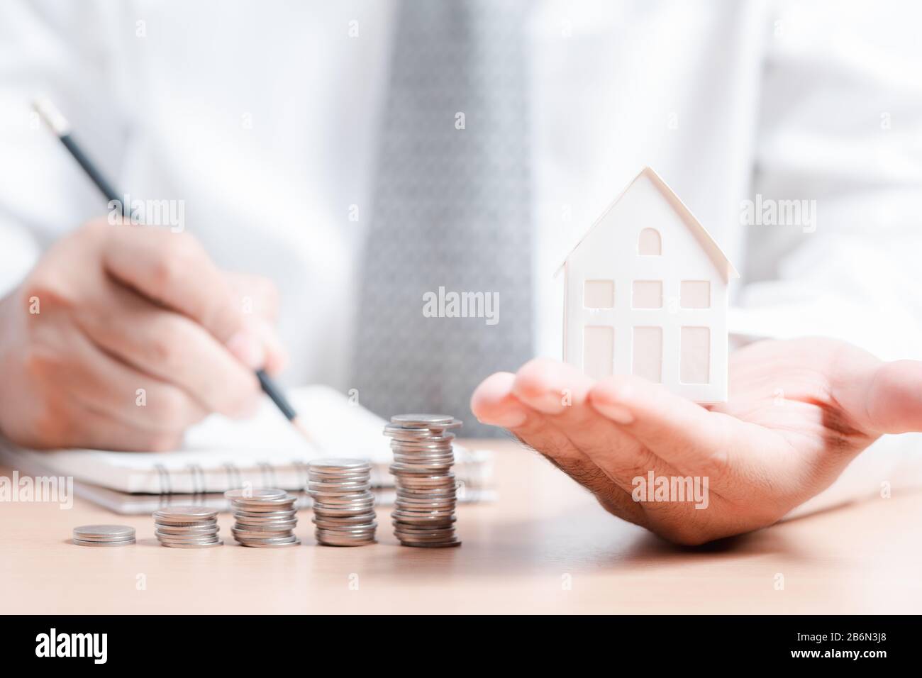 Saving money concept. Business man hand holding house model with Row of ...