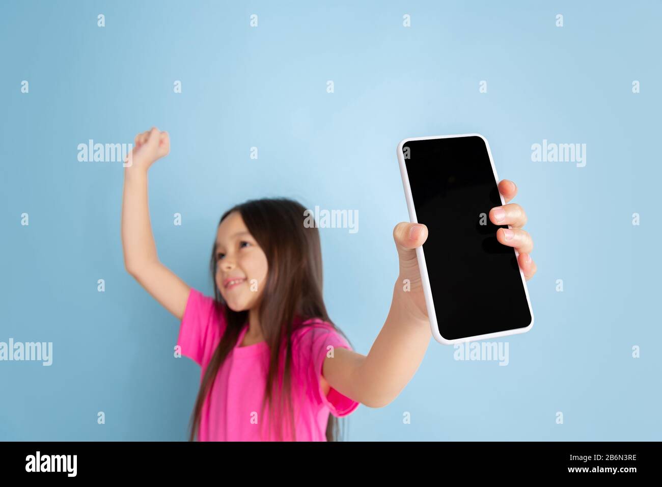 Showing phone's screen. Caucasian little girl's portrait on blue studio ...