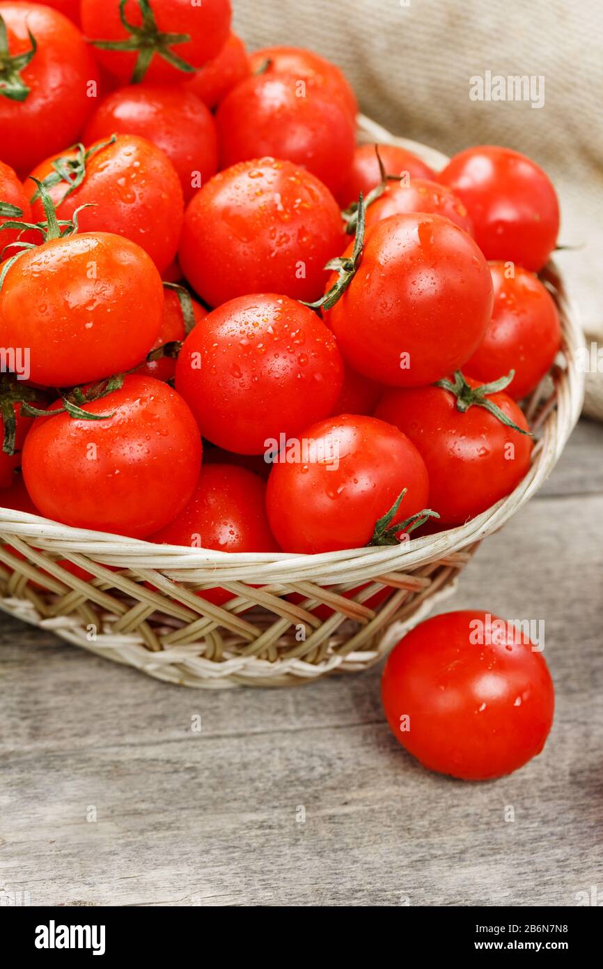 Small red tomatoes in a wicker basket on an old wooden table. Ripe and ...