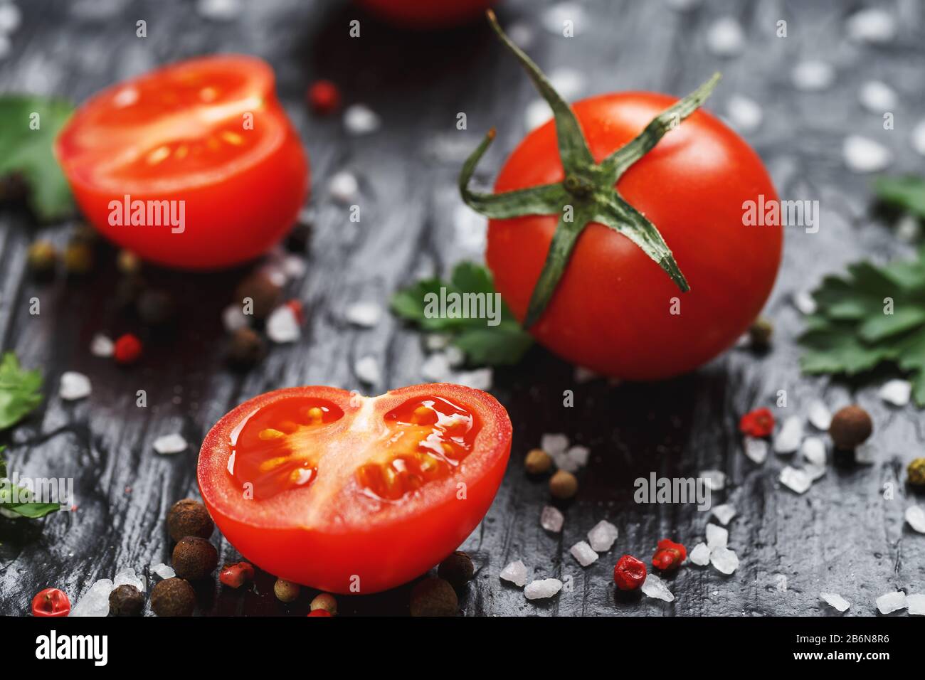 Fresh Sliced Cherry Tomatoes on a black background with spices coarse ...
