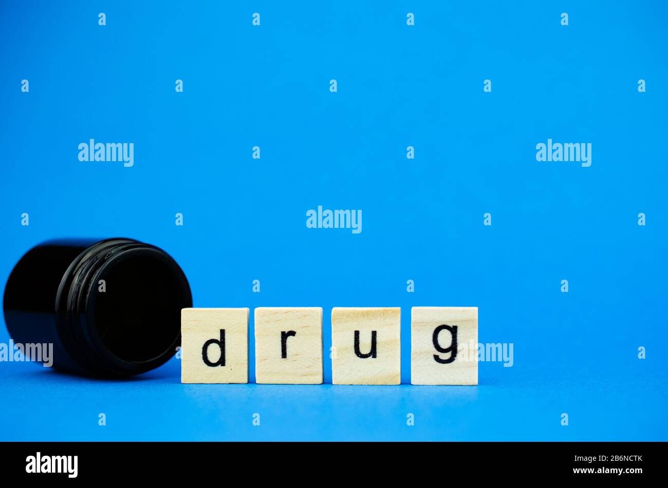 The word DRUG on wooden cubes and a medical dark flask on a blue ...