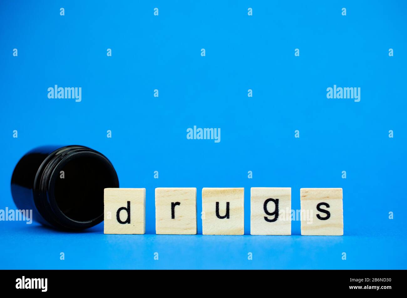 The word DRUGS on wooden cubes and a medical dark flask on a blue ...