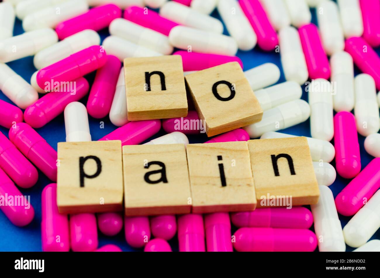 The word NO PAIN on the background of scattered pink and white capsules ...
