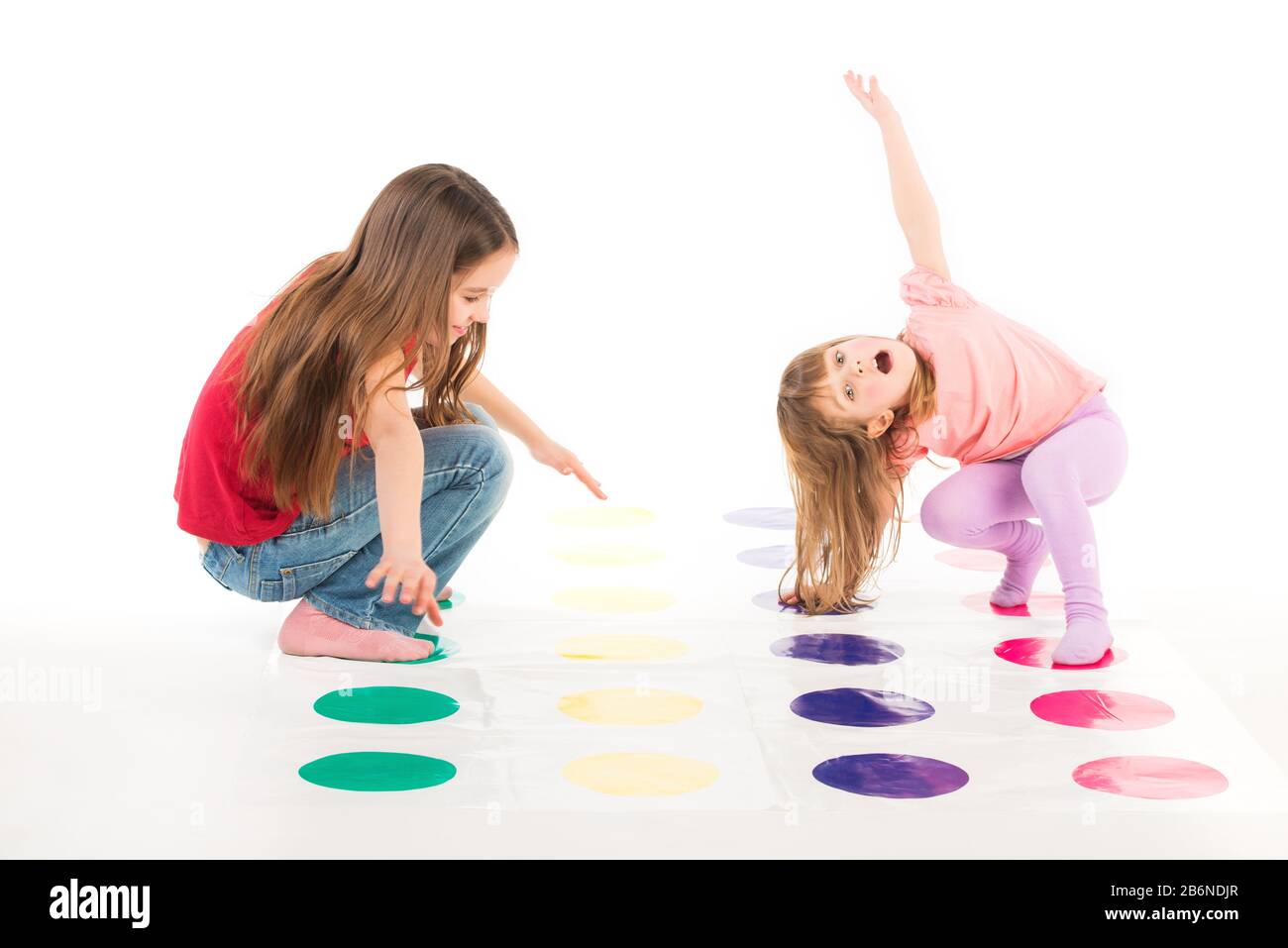 Two happy girls in children's clothes enthusiastically play a Twister ...