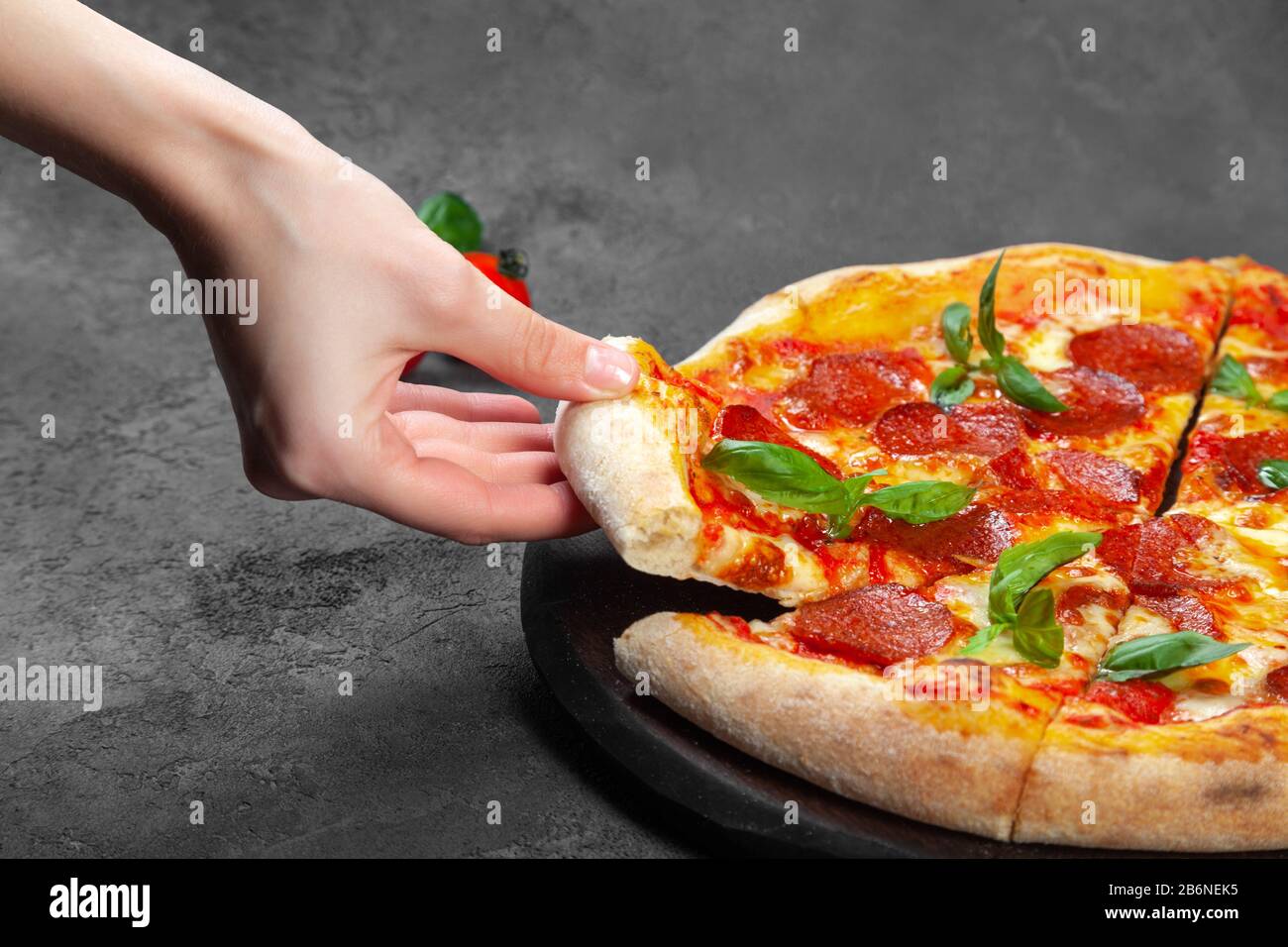 Female hand take slice of fresh pepperoni pizza with basil, cherry ...