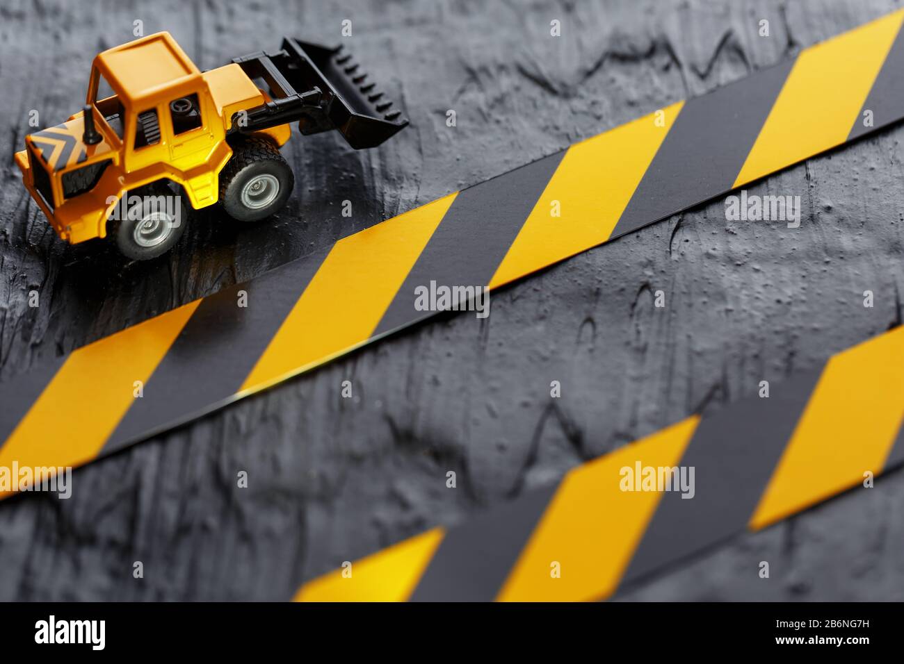 Yellow toy bulldozer on a black background texture. Black and yellow ...