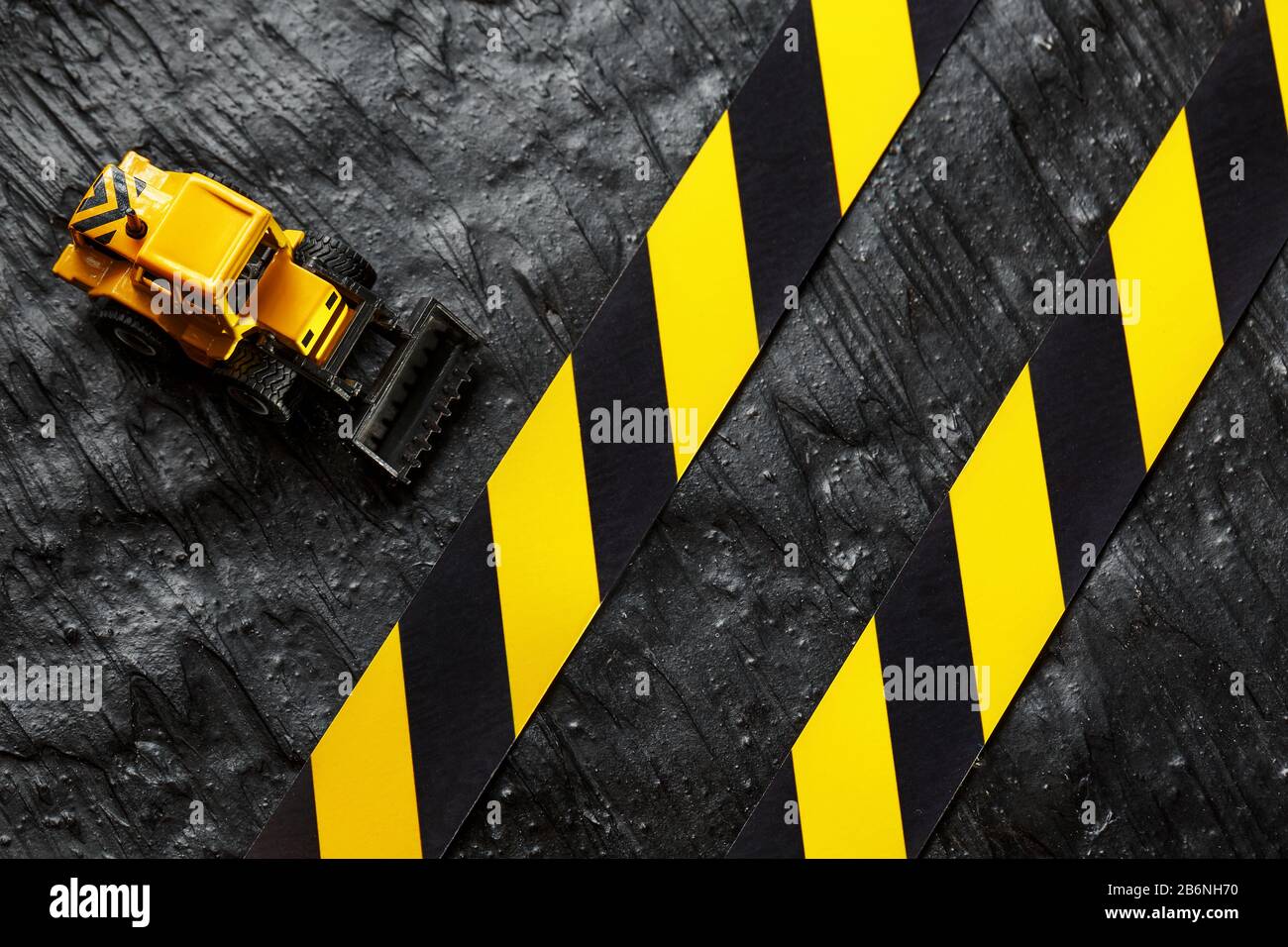 Yellow toy bulldozer on a black background texture. Black and yellow ...