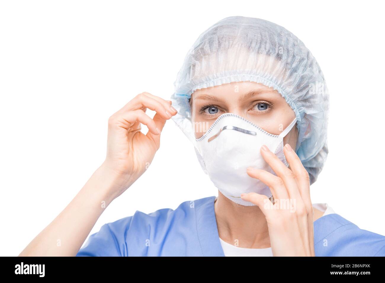 Portrait of blue-eyed woman in surgical cap putting respiratory mask on ...