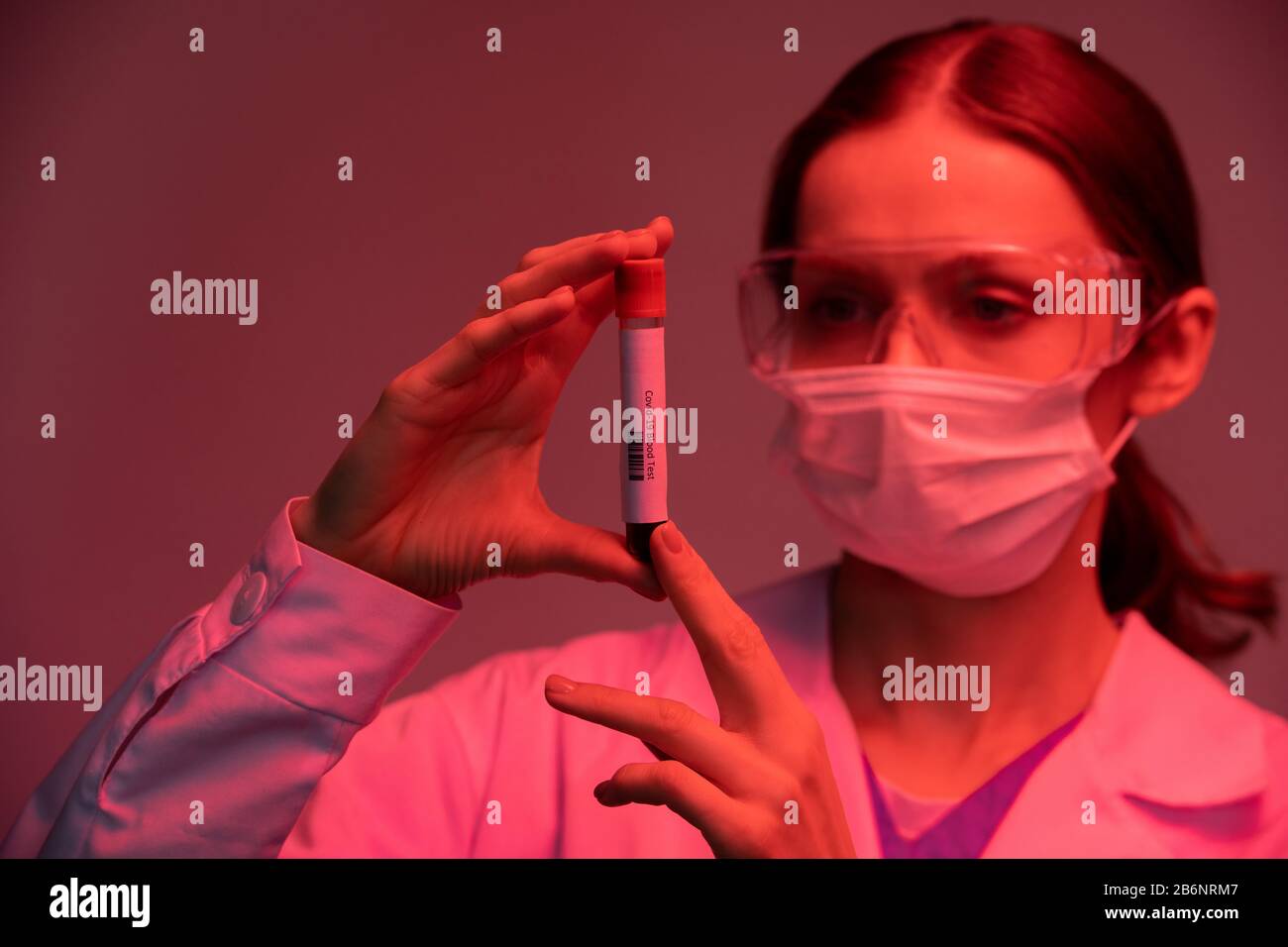 Medical scientist in face mask and safety goggles holding test tube ...