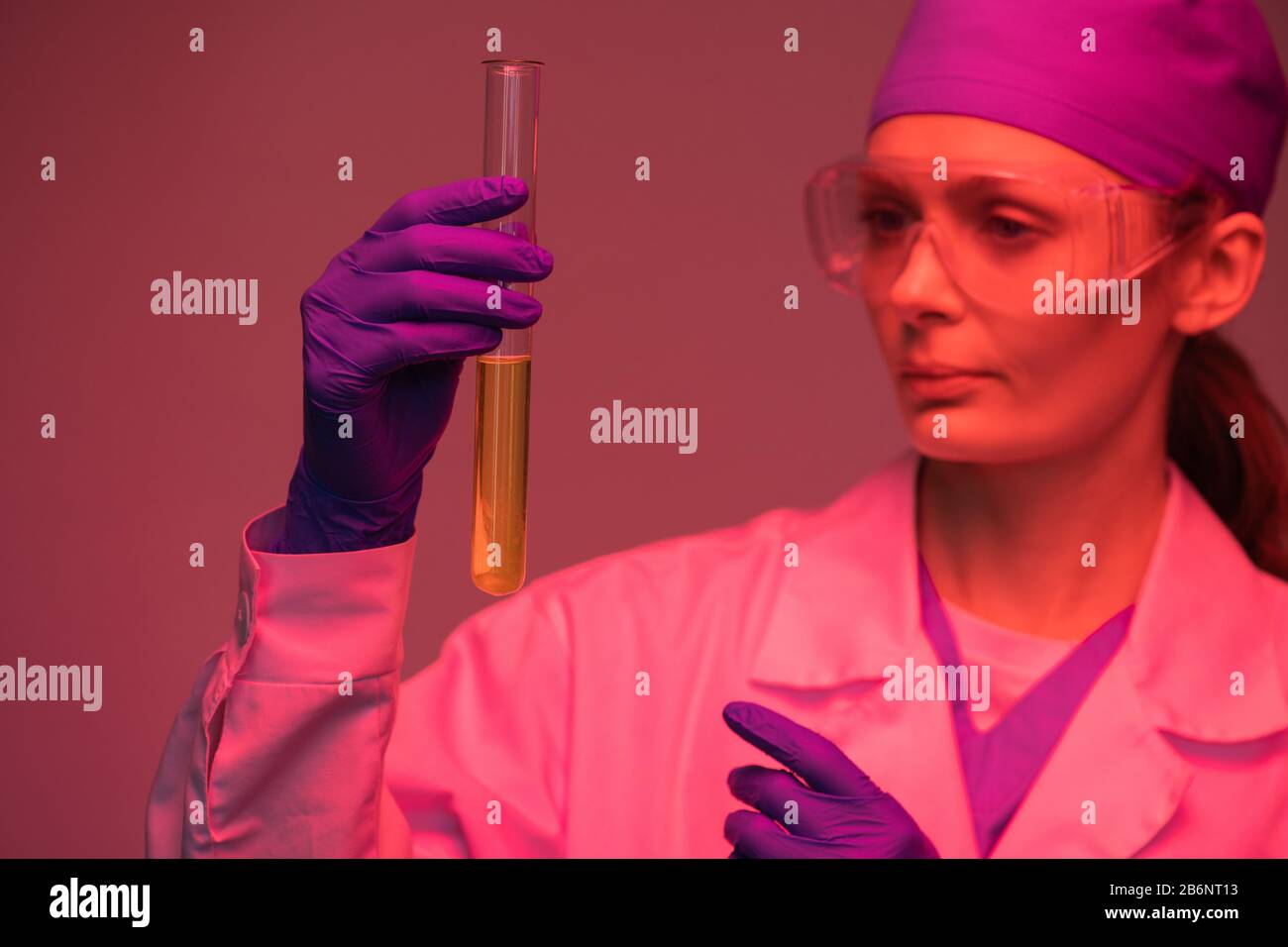 Serious female laboratory technician in gloves holding long test tube ...
