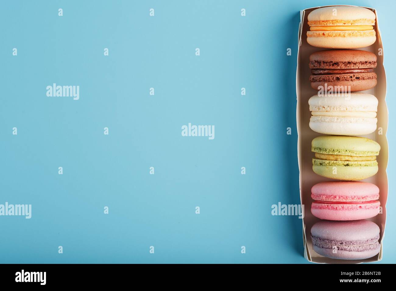Macaroni cookies of different colors in a white box on a blue ...
