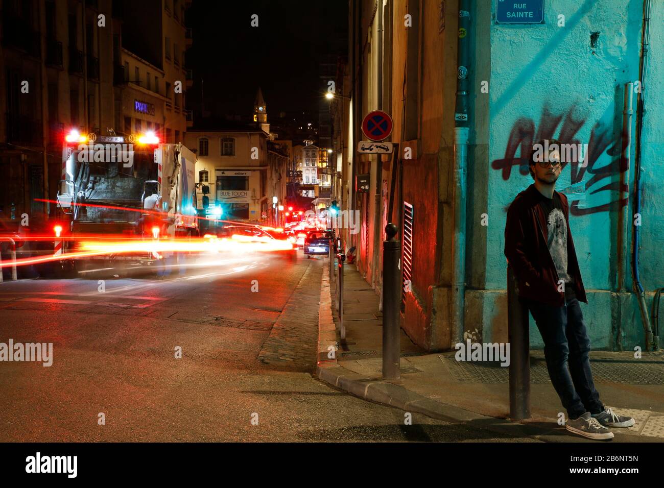 Male model leaning on a pole with fading car lights in the background ...