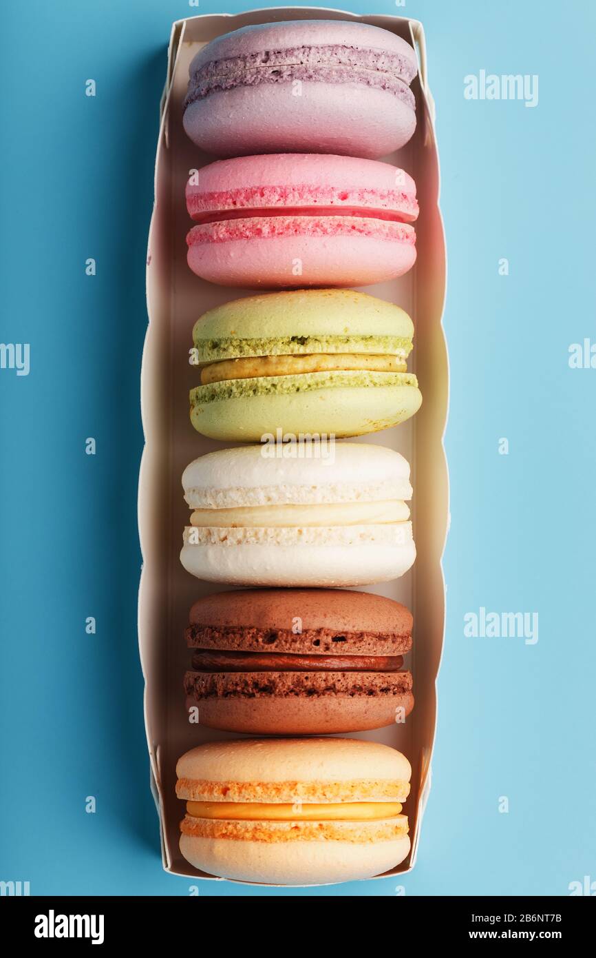Macaroni cookies of different colors in a white box on a blue ...