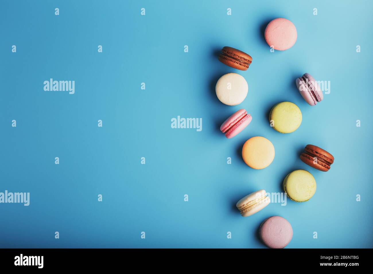 Macaroni cookies of different colors are scattered on a blue background ...