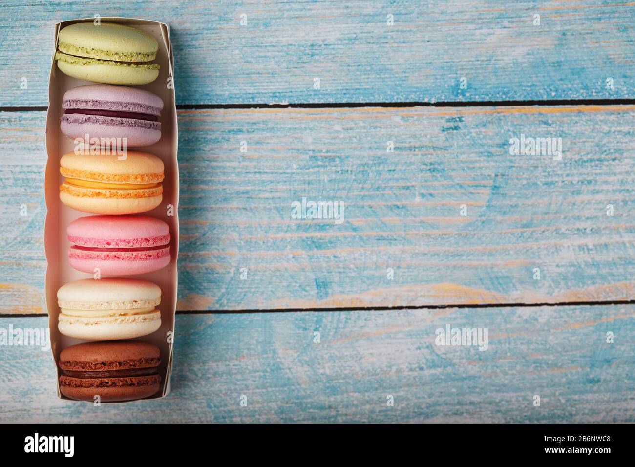 Macaroni cookies of different colors in a box on a blue, old wooden ...