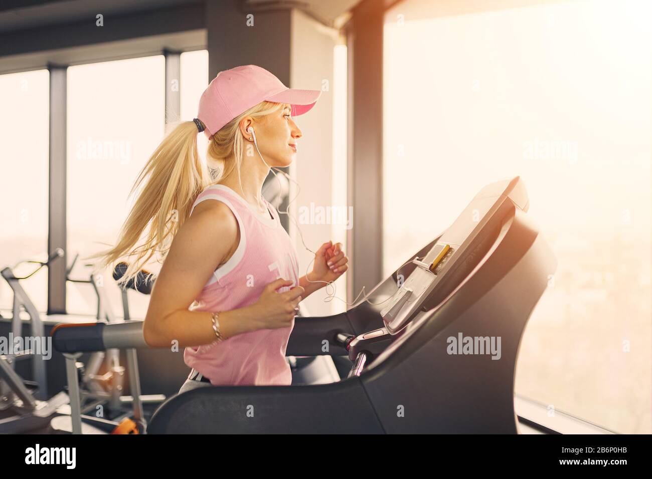 Side view of sporty blonde woman in pink cap exercising on treadmill in gym Stock Photo - Alamy