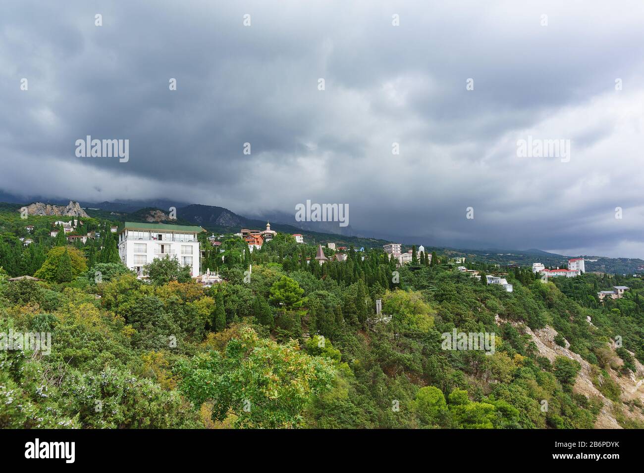 Roofs of houses are seen among pines and cypresses on the slope of the ...