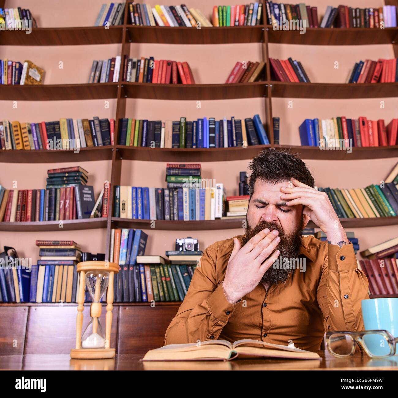 Man on yawning face reading book, studying, bookshelves on background ...
