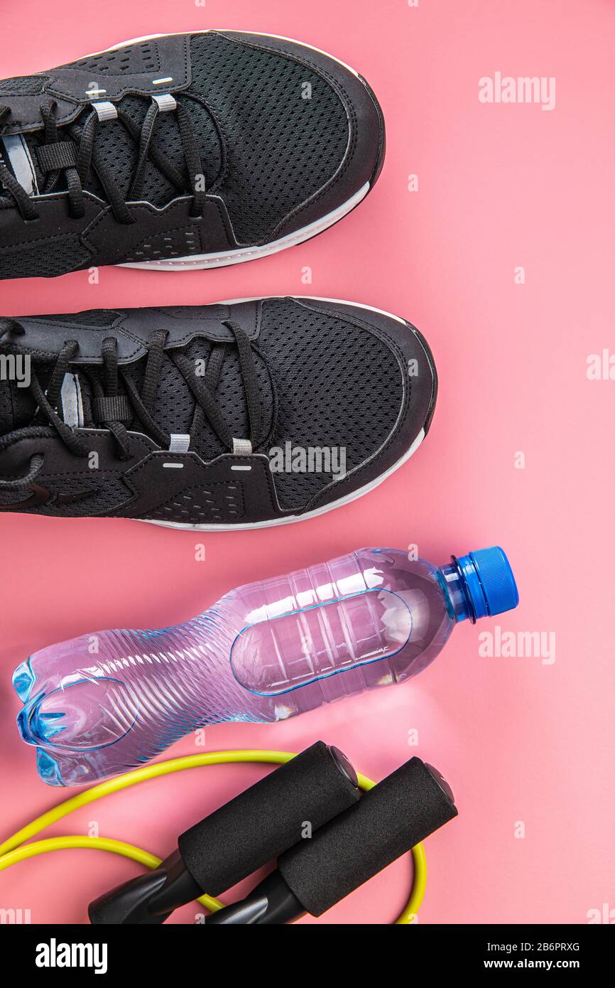 Black sport shoes, jump rope and bottle of water on pink background ...