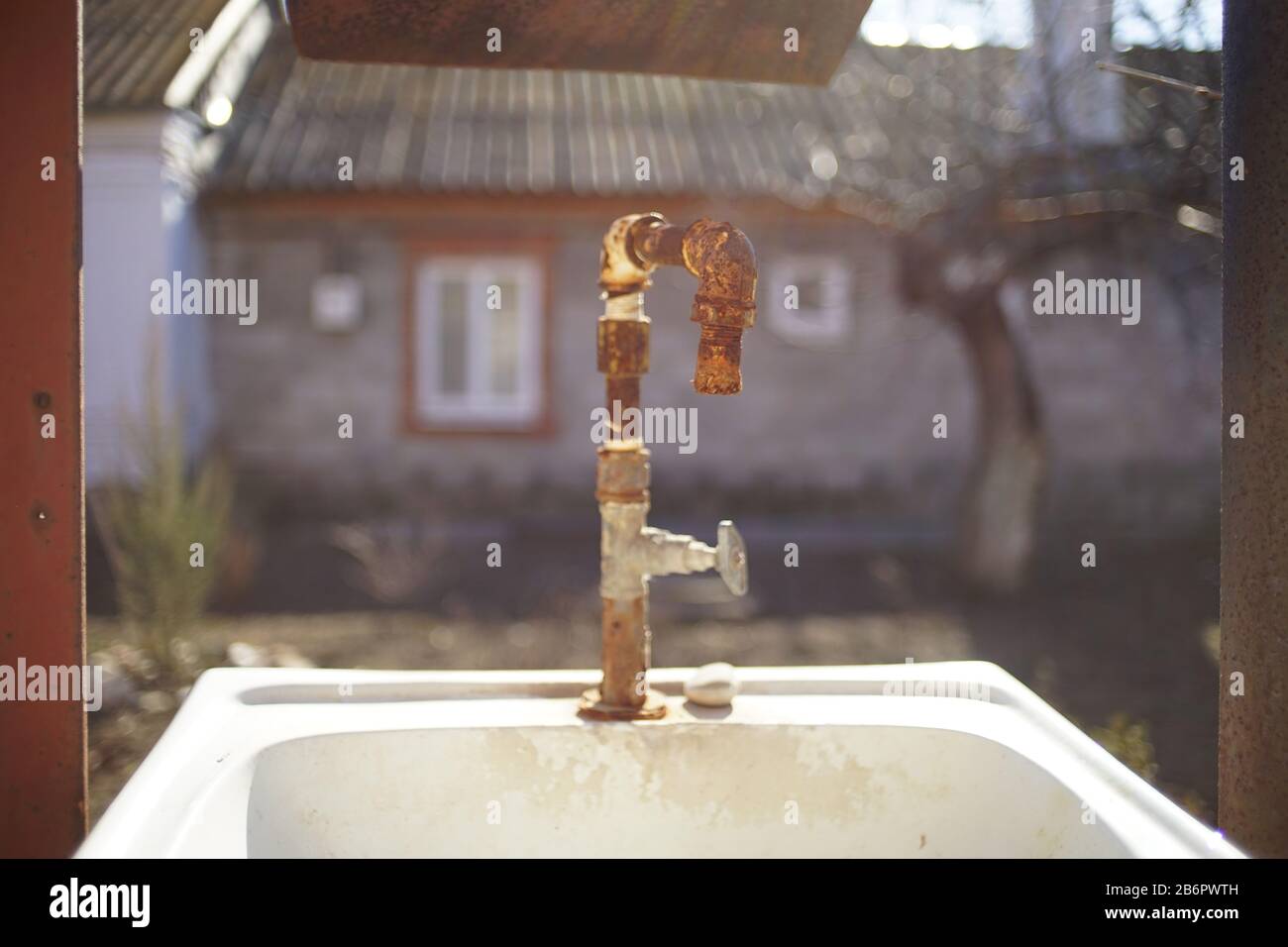 Old rusty faucet on a sink in a rural yard. The facade of the house in ...