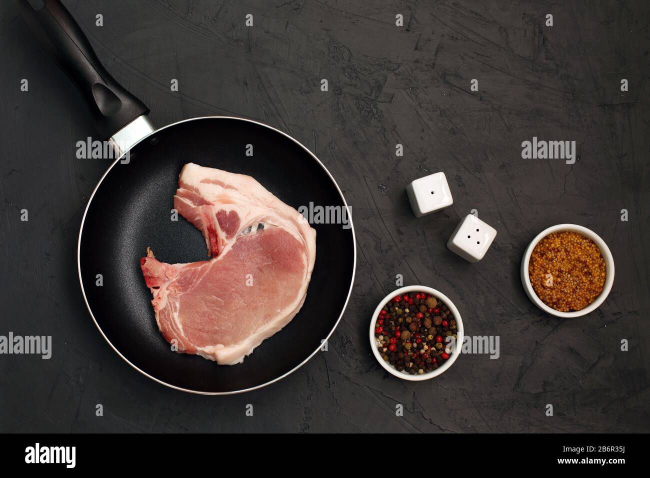 Raw pork loin chops in rustic skillet on black background Stock Photo ...