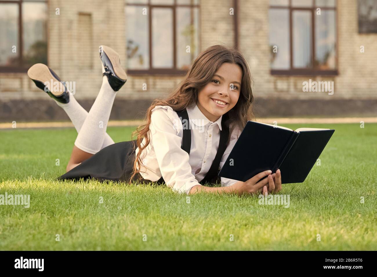 After-school lesson. Small girl read lesson book on green grass. Happy ...