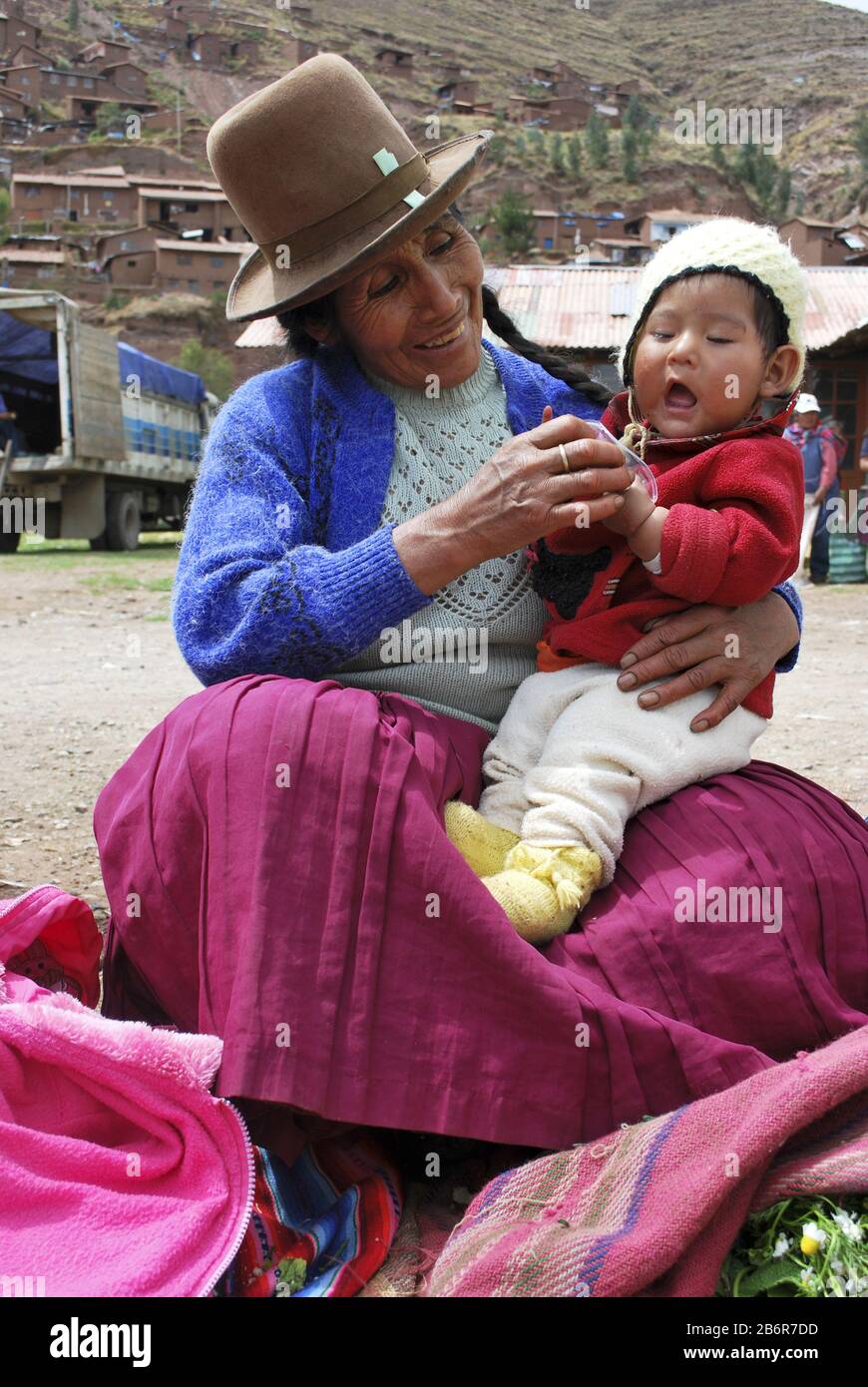 Cusco, Peru. Typical Peruvian lady with hat on feeds baby on her lap ...