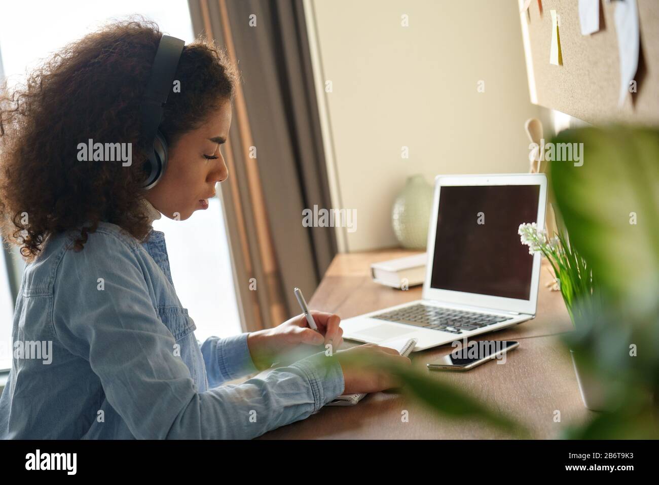 Focused african female student wear headphones elearning making notes ...