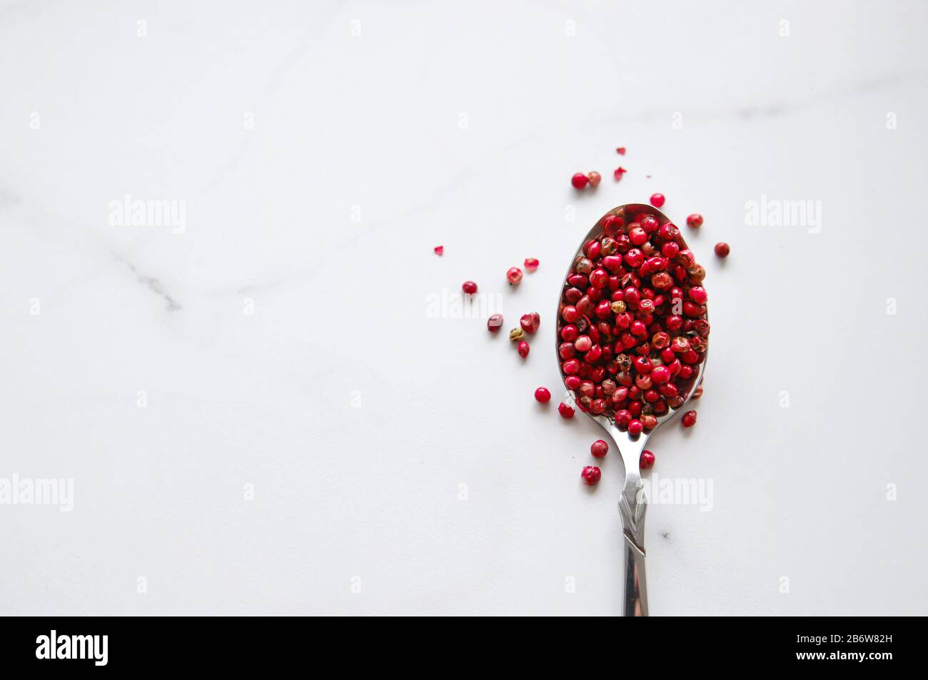 Pink pepper is spoon on marble background. Close up and top view spice ...