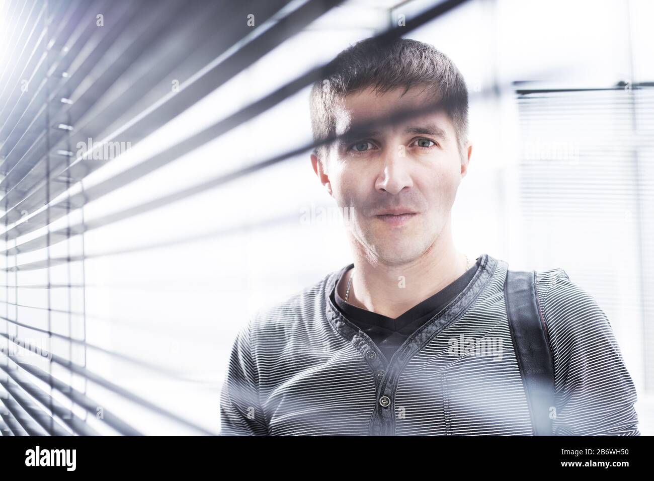 serious young man looking through window blind Stock Photo - Alamy