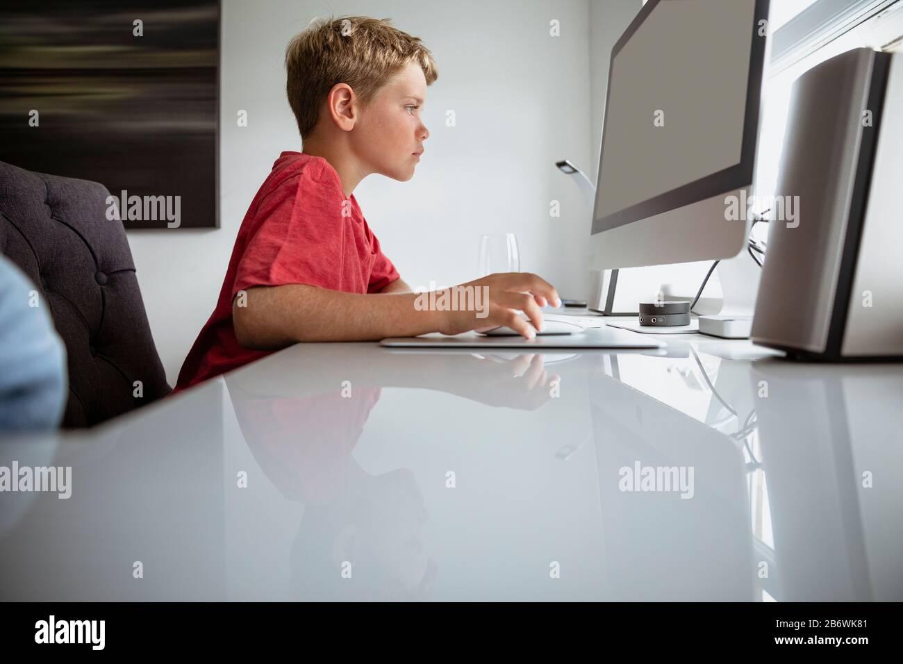 A side-view shot of a young boy sitting down at a desk using a computer ...