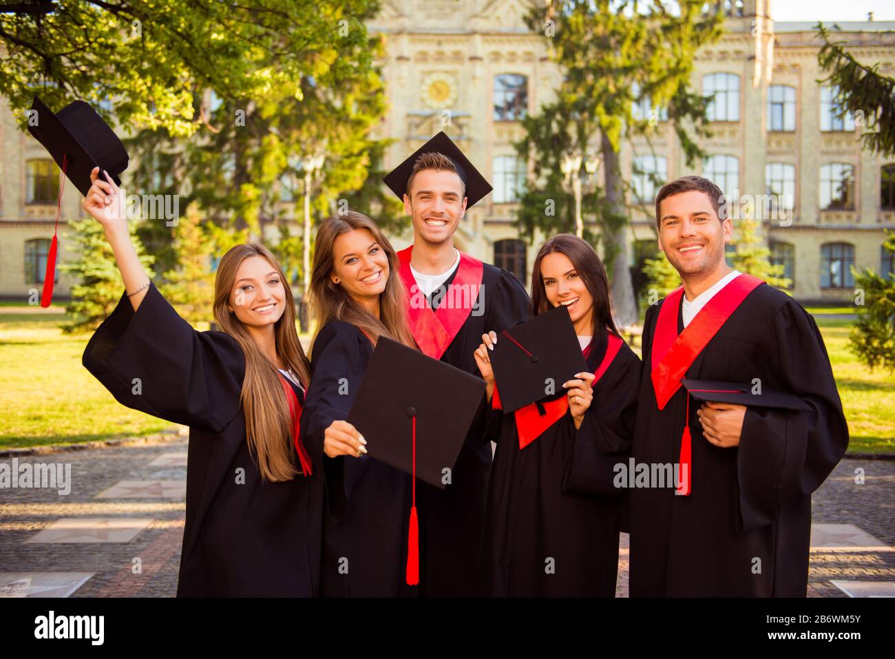 successful happy five graduates in robes and hats with tassel together ...