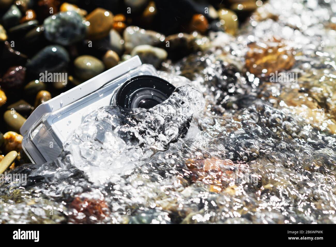 White action camera with underwater case in water on the pebble beach ...