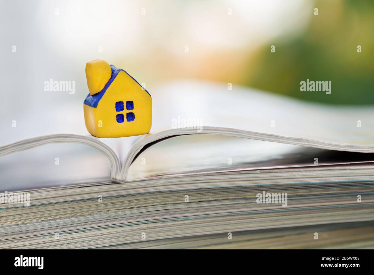 Miniature yellow toy house on an open magazine and green blurry ...