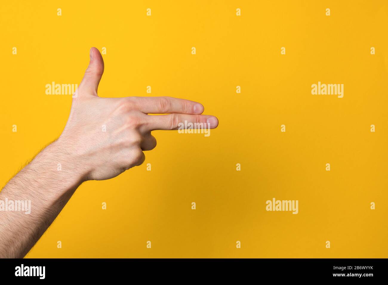 man hand imitating gun over a wide yellow background with copyspace ...
