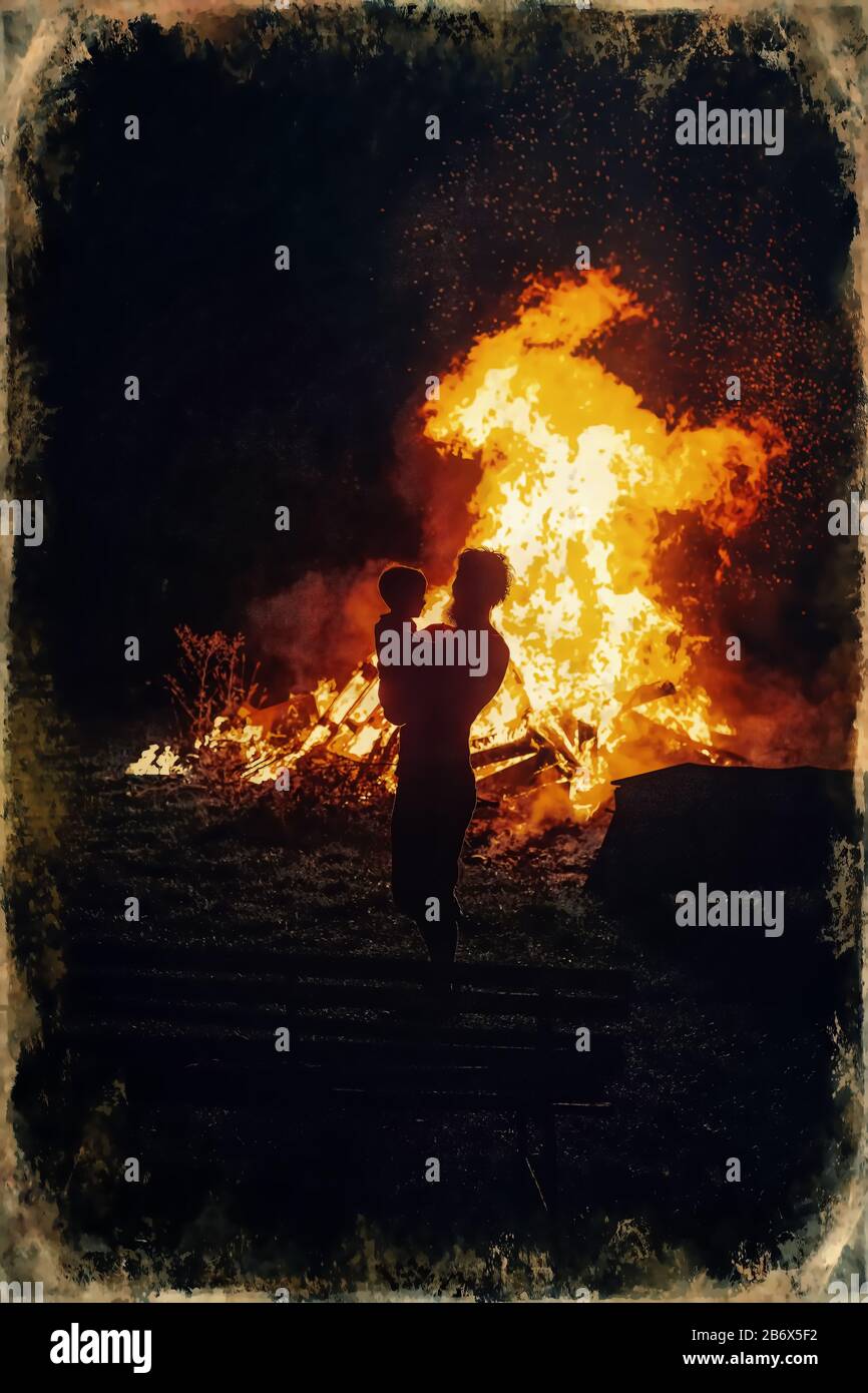 father holding his little son with burning bonfire on background ...