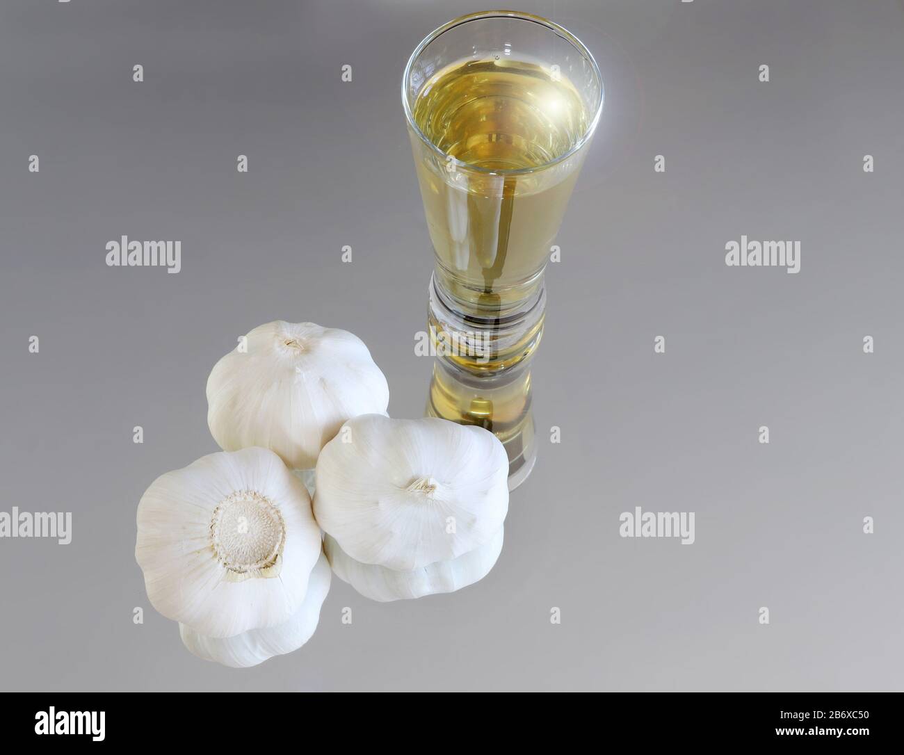 Garlic bulbs and garlic cloves on a mirror with a glass of alcohol ...