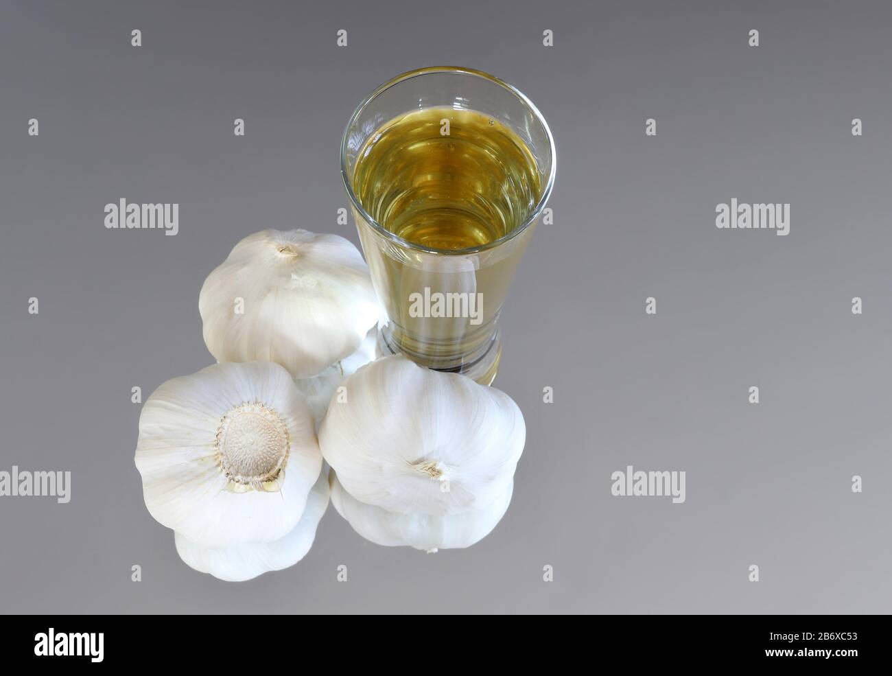 Garlic bulbs and garlic cloves on a mirror with a glass of alcohol ...