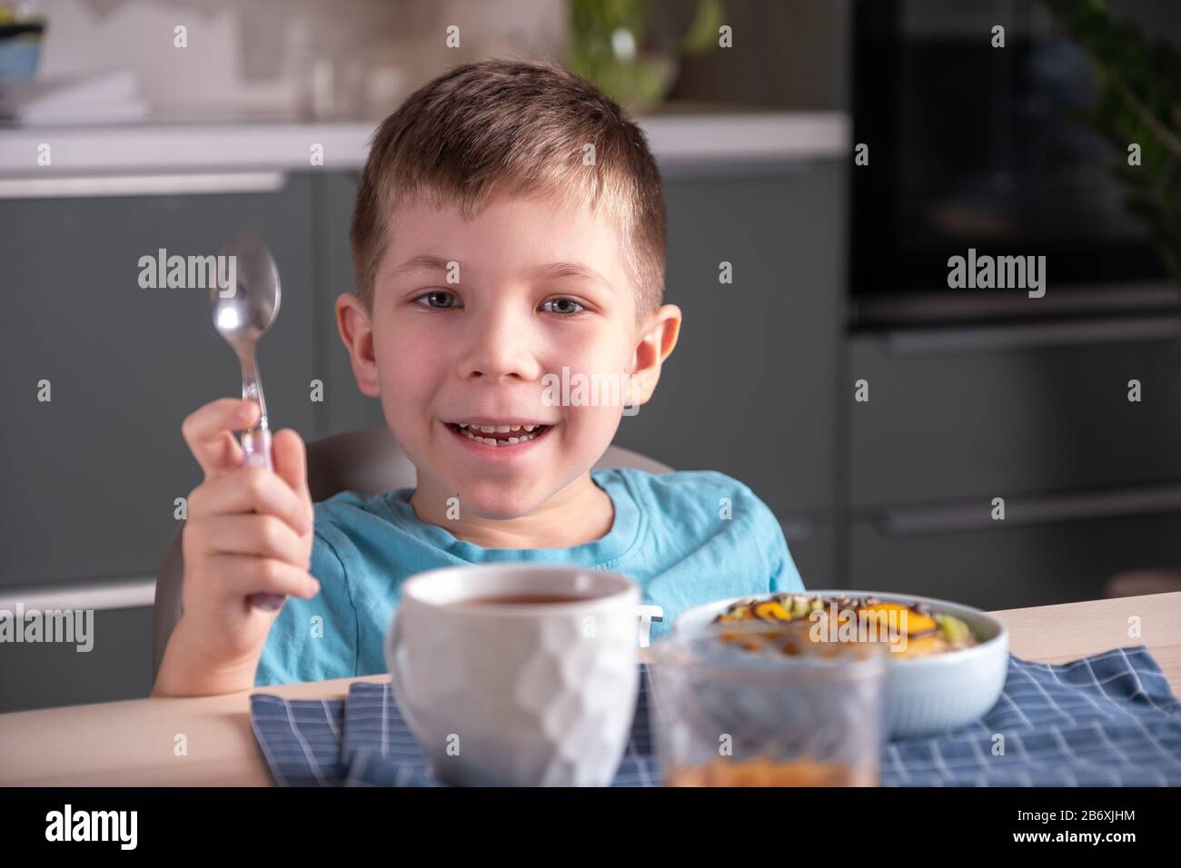 Cute boy sitting at the table and eating oatmeal porridge. Happy child ...