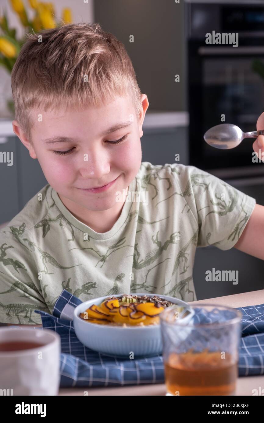 Cute boy sitting at the table and eating oatmeal porridge. Happy child ...