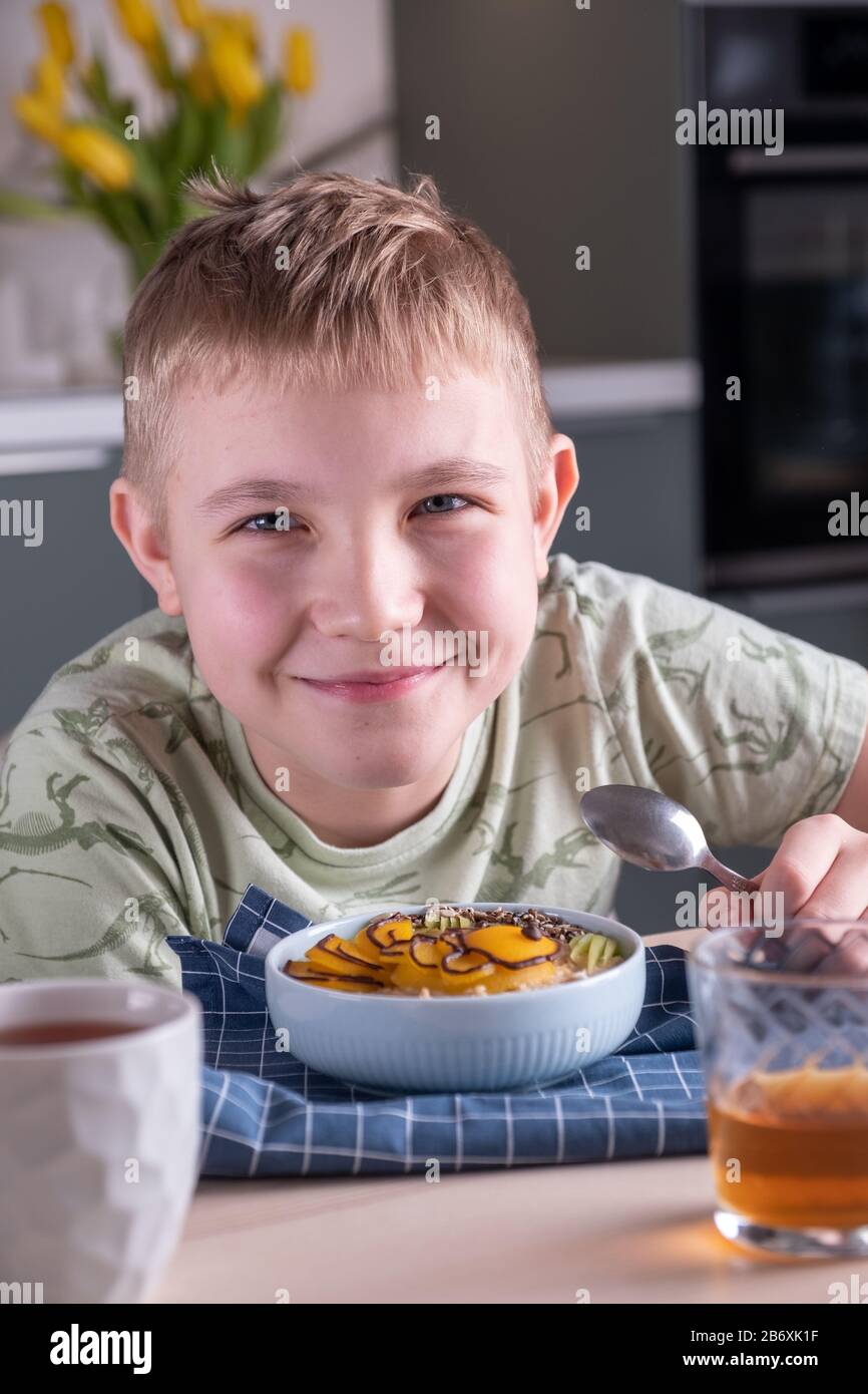 Cute boy sitting at the table and eating oatmeal porridge. Happy child ...