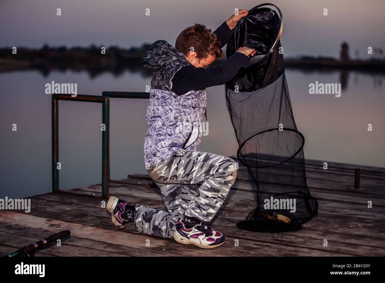 Cute little boy fishing on a lake in the evening and showing catch fish ...