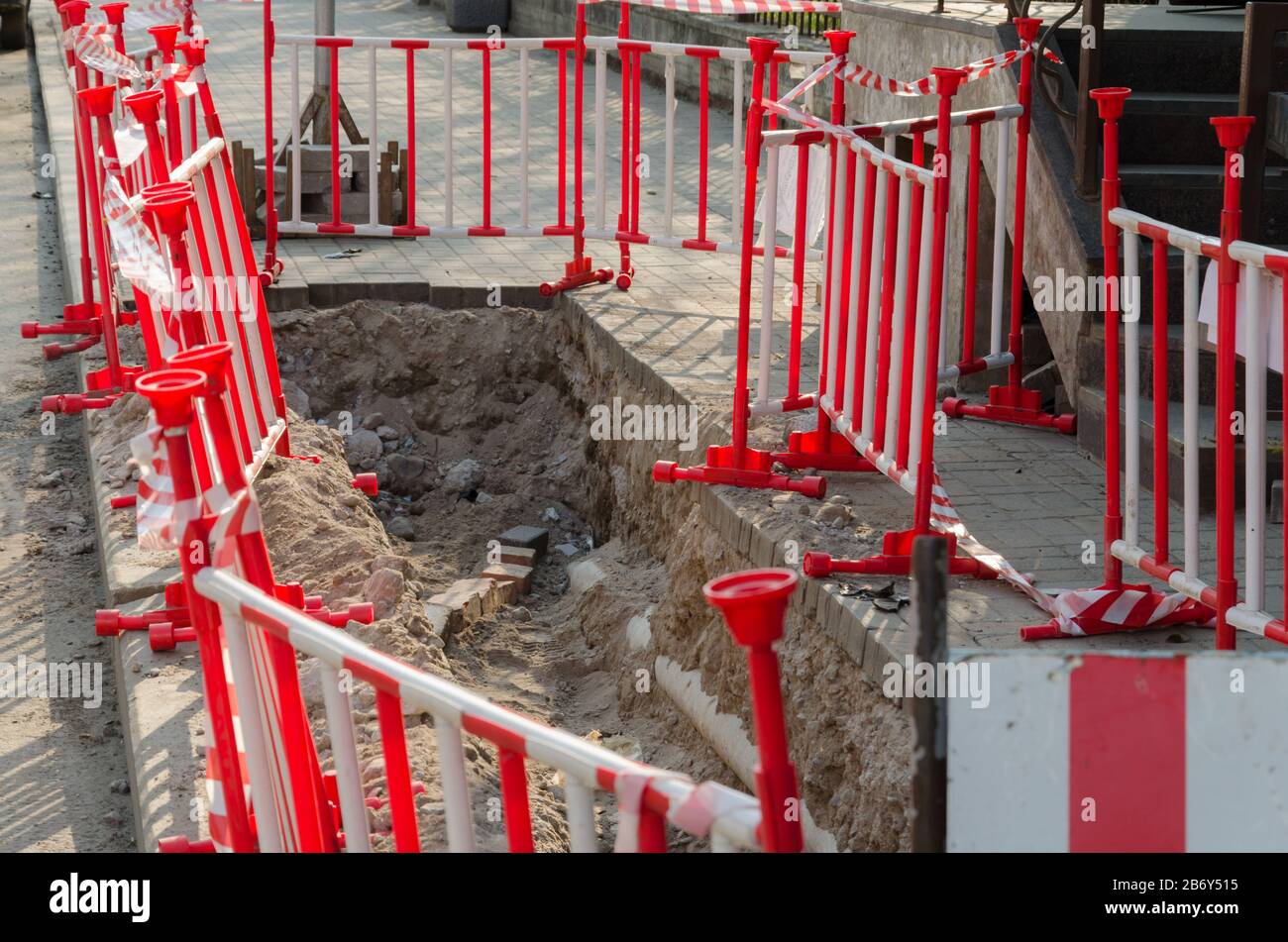 Dangerous pit on the sidewalk surrounded by warning red-and-white ...