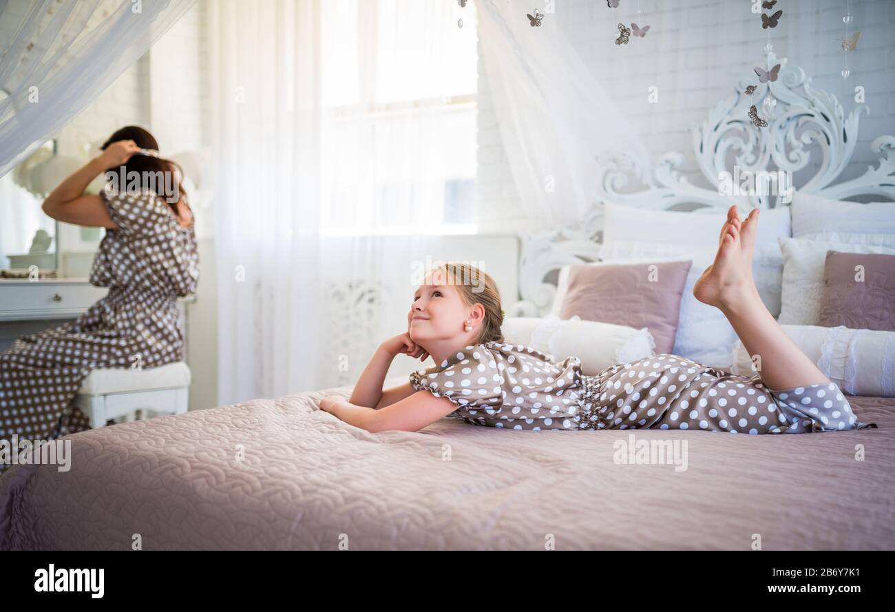 Pensive little girl in a long dress lies on the bed against the ...