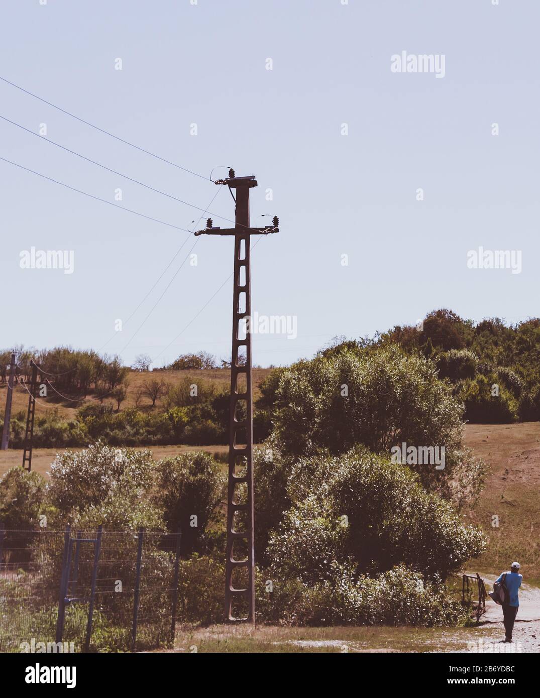 Man walking on gravel road near high voltage power lines on power pylon ...