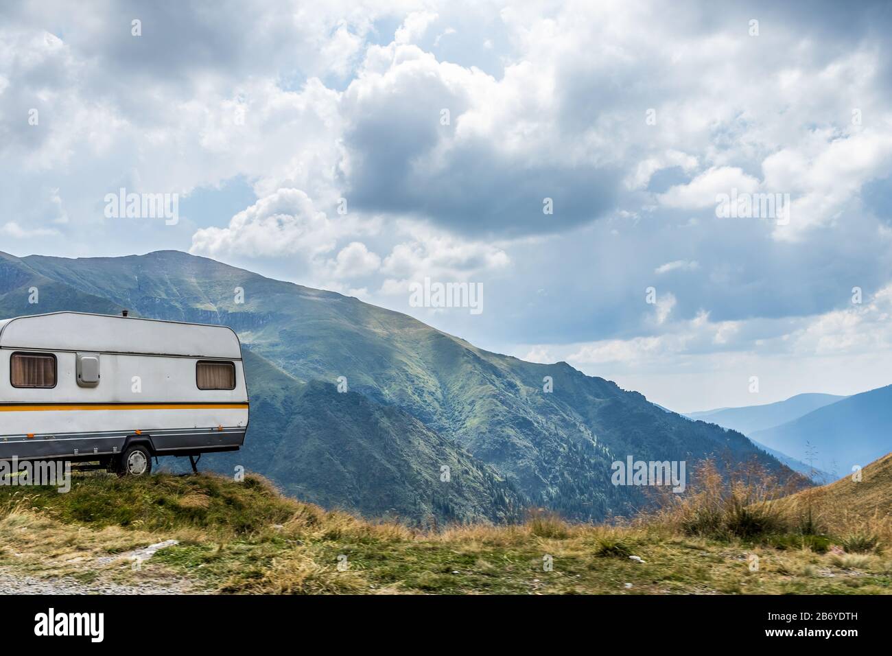 Caravan parked on the ledge of a mountain road with mountains in the ...
