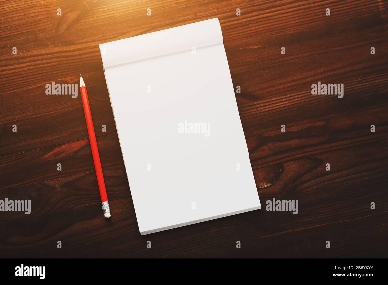 Notebook with a red pencil on a brown background with warm sunlight ...