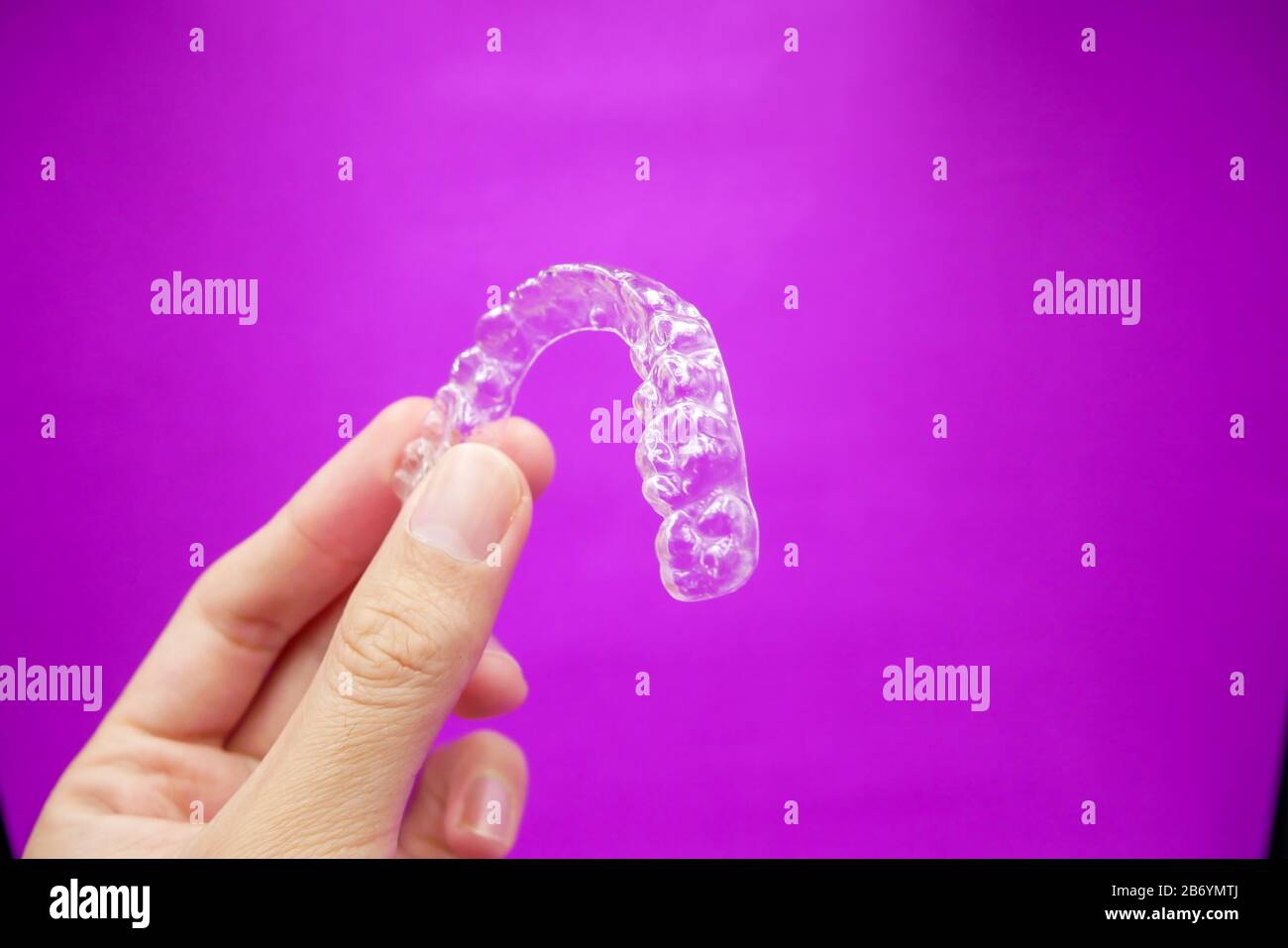 hand holding clear plastic retainer teeth that isolated on purple ...