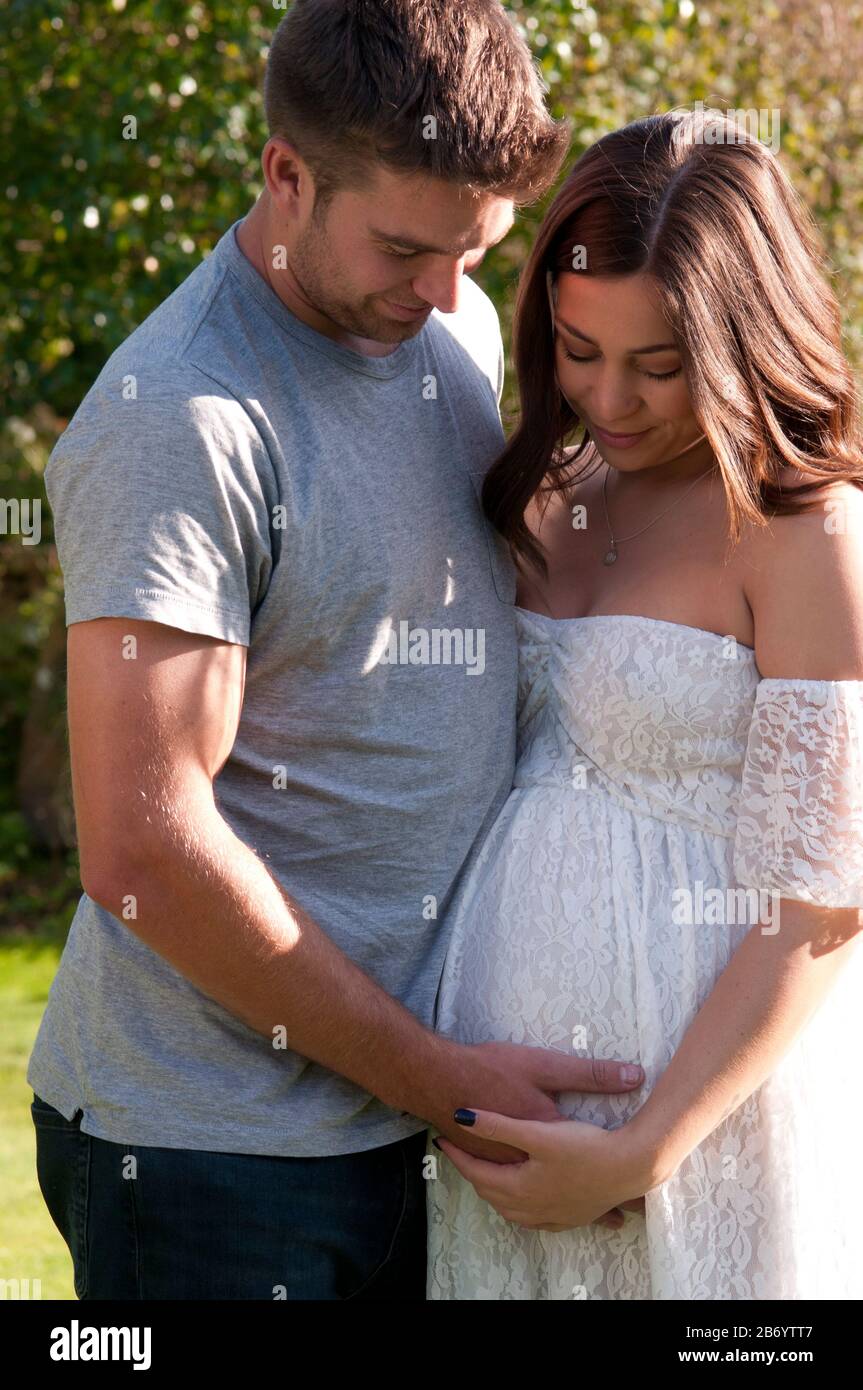 Beautiful pregnant young woman and her partner with their arms around ...