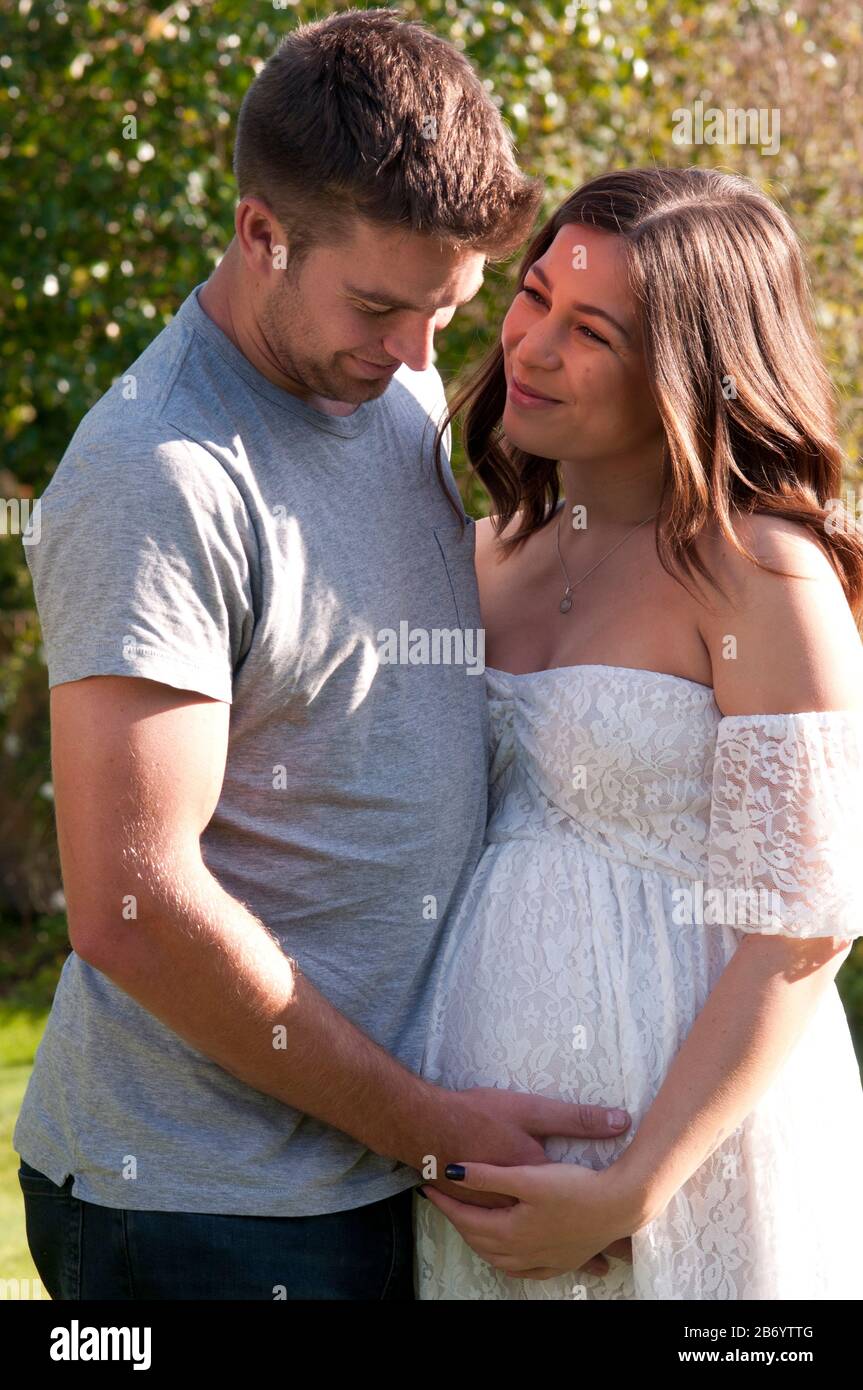 Beautiful pregnant young woman and her partner with their arms around ...